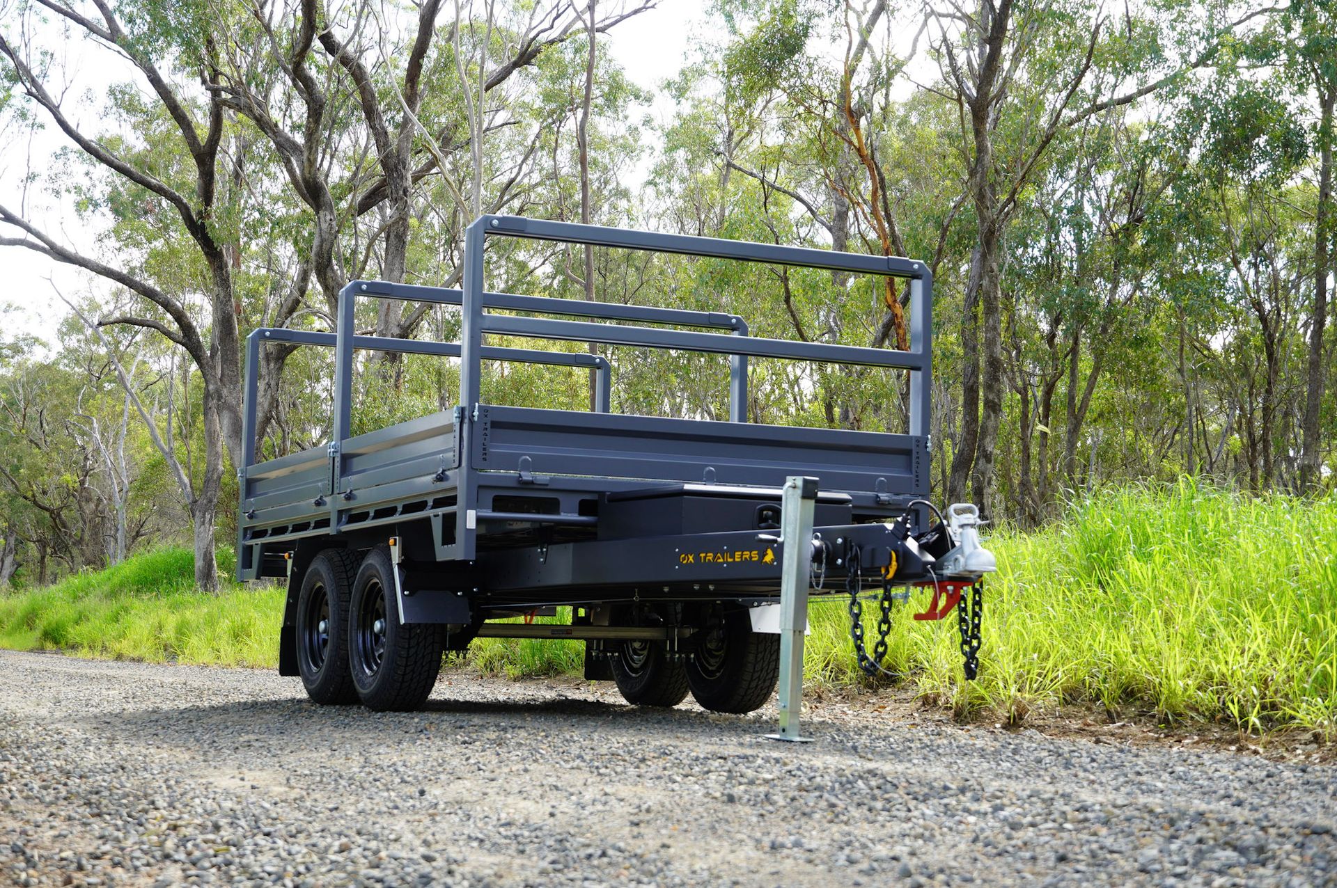 The Ox Pro Series Flat Top Trailer with a drawbar toolbox and ladder rack set on a dirt road.